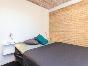 Quarto com cama, mesa de cabeceira, abajur e parede de tijolos.