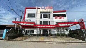 Um edifício com fachada vermelha e branca, um letreiro com a inscrição "i jalak guest house" e um estacionamento na frente.