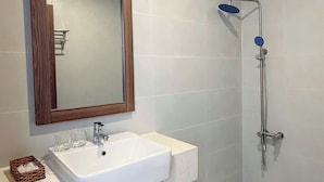 Casa de banho com lavatório branco, espelho com moldura de madeira e chuveiro com barra de mão.