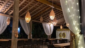 Área de refeições ao ar livre com luminárias pendentes e cortinas esvoaçantes.