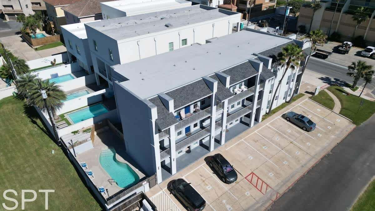 Um edifício com vários andares, piscina no terraço, área de estacionamento e vista clara do bairro ao redor.