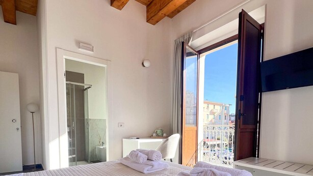 Quarto com cama grande, banheiro e vista da cidade por uma janela ampla.