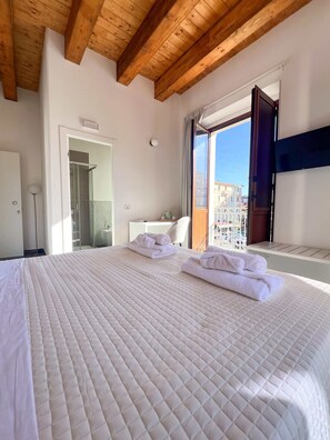 Quarto com cama grande, banheiro e vista da cidade por uma janela ampla.
