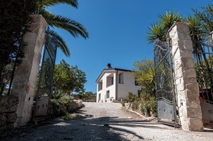 Uma casa de dois andares com portão de entrada de pedra, cercada por palmeiras e plantas.