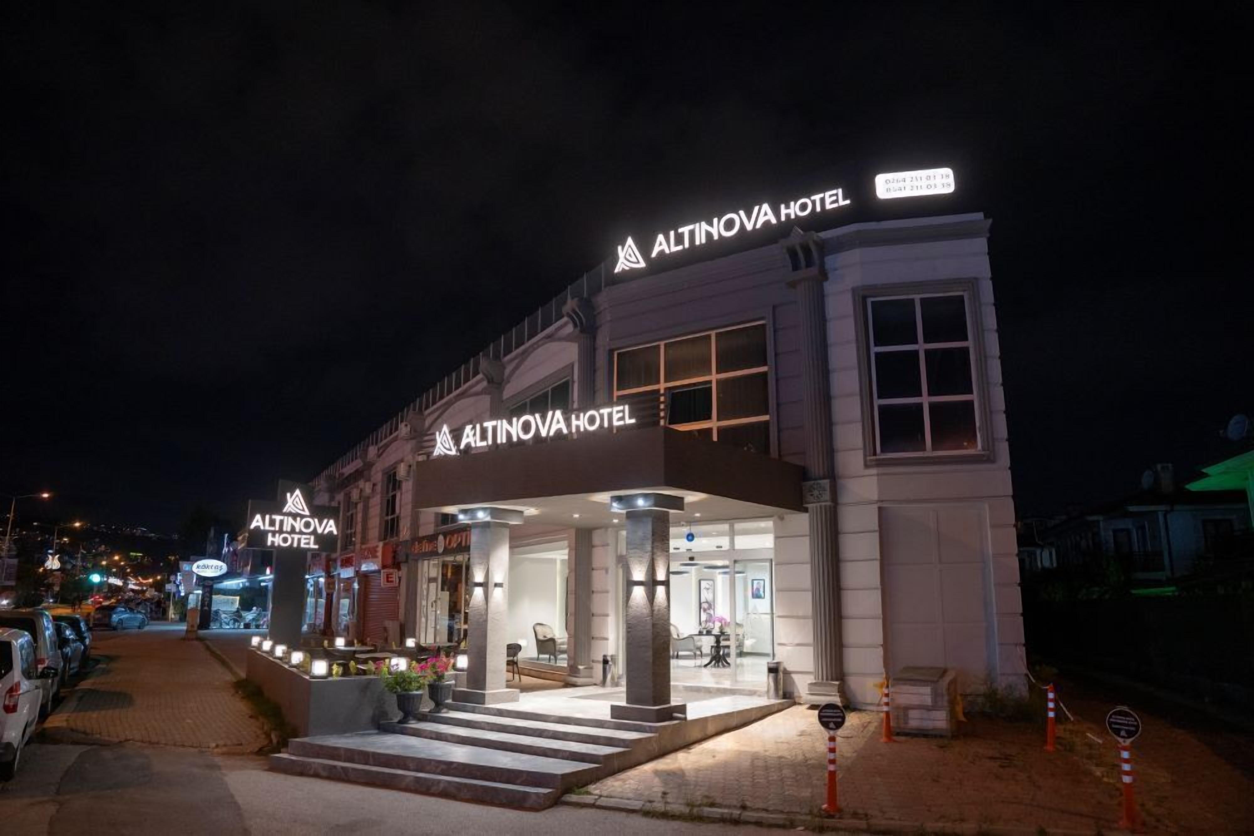 Exterior do Hotel Altinova à noite, com entrada bem iluminada, degraus que levam à porta, área de recepção visível e estacionamento com carros.