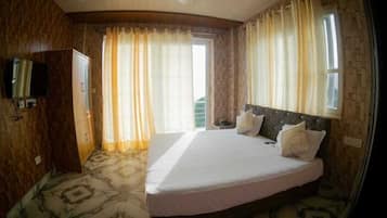 Quarto de hotel com uma cama grande, cortinas, uma televisão e um chão estampado.