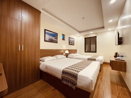 Quarto de hotel com duas camas, guarda-roupa de madeira, televisão e janela com vista.