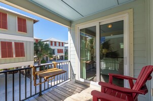 Um deck de madeira com mesa e cadeiras, uma porta de vidro que dá para uma área coberta e vista para edifícios vizinhos.