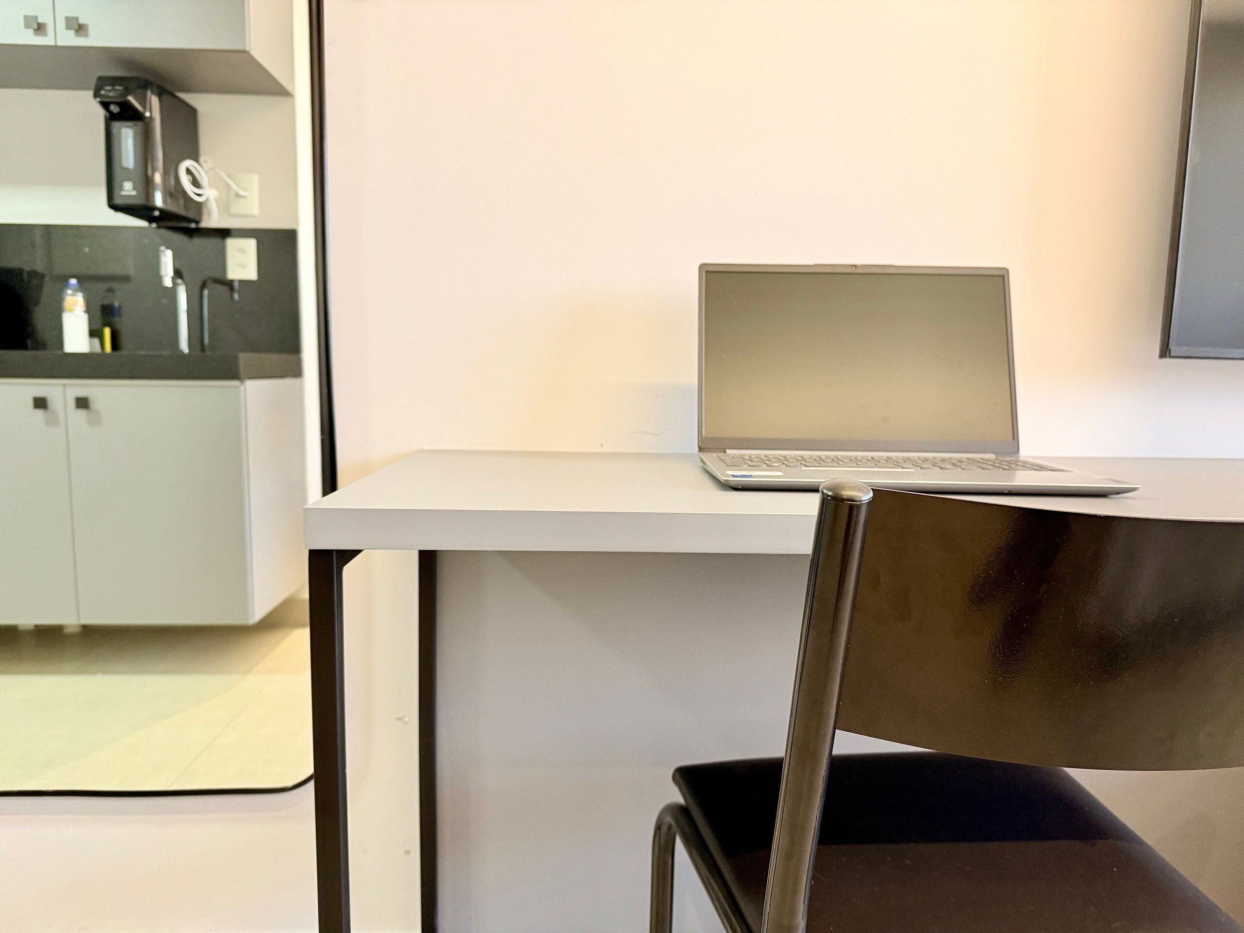 Uma cozinha moderna com um laptop sobre uma mesa branca, uma cadeira e uma máquina de café.