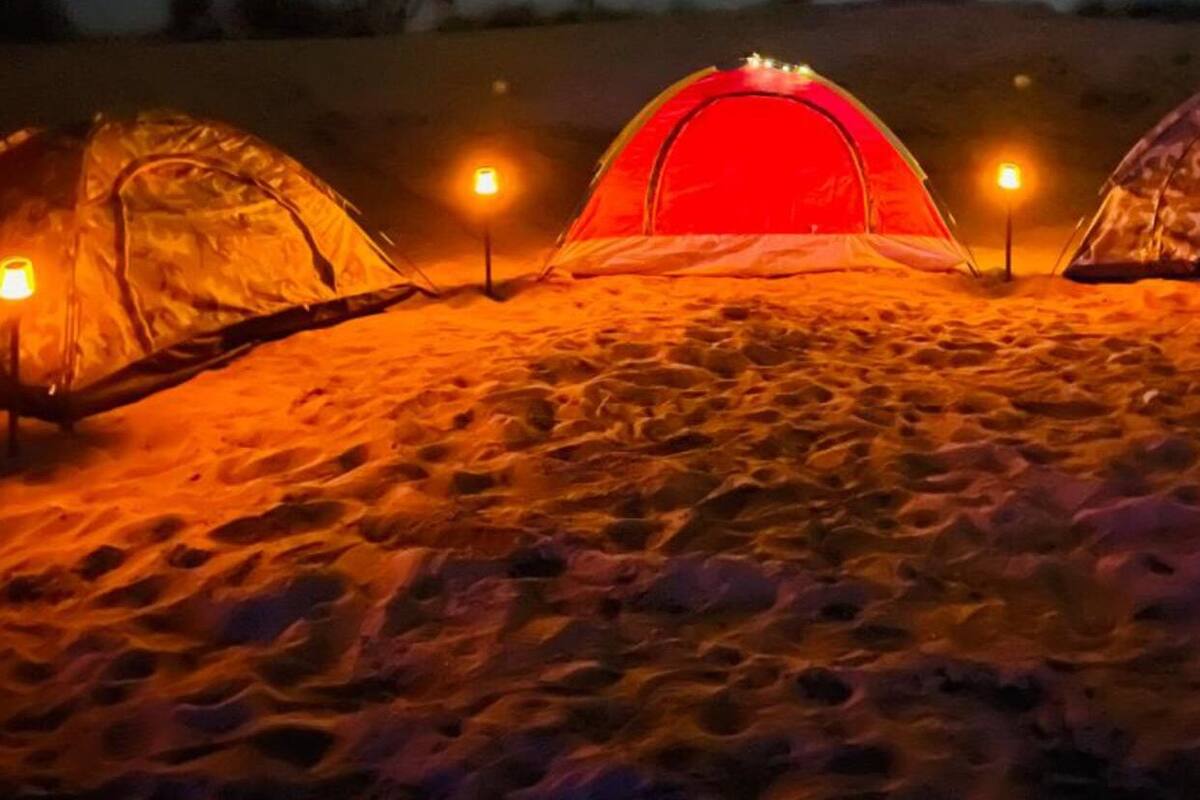 Três tendas sobre um terreno arenoso, com luzes no interior.