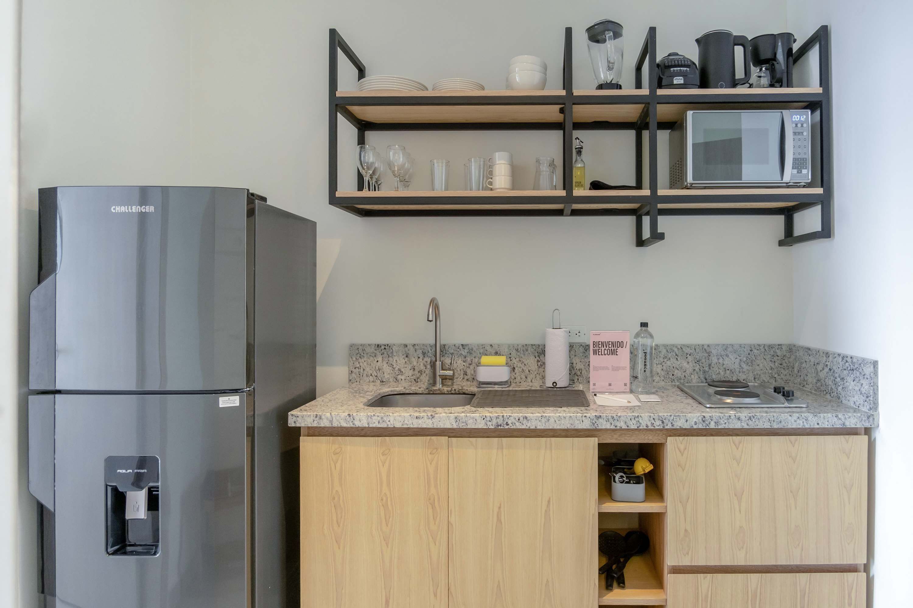 Uma cozinha equipada com geladeira, micro-ondas, pia e prateleiras com louças e utensílios.