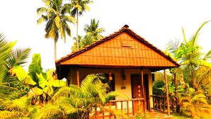 Uma casa pequena, térrea, com telhado de cerâmica, rodeada por vegetação tropical exuberante.
