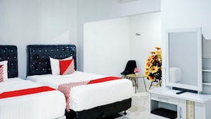 Quarto de hotel com duas camas, televisão, uma pequena mesa com um vaso de flores e um armário branco.
