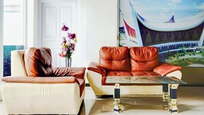 Um quarto com um sofá bege, um sofá de couro marrom e uma pequena mesa com um vaso de flores.