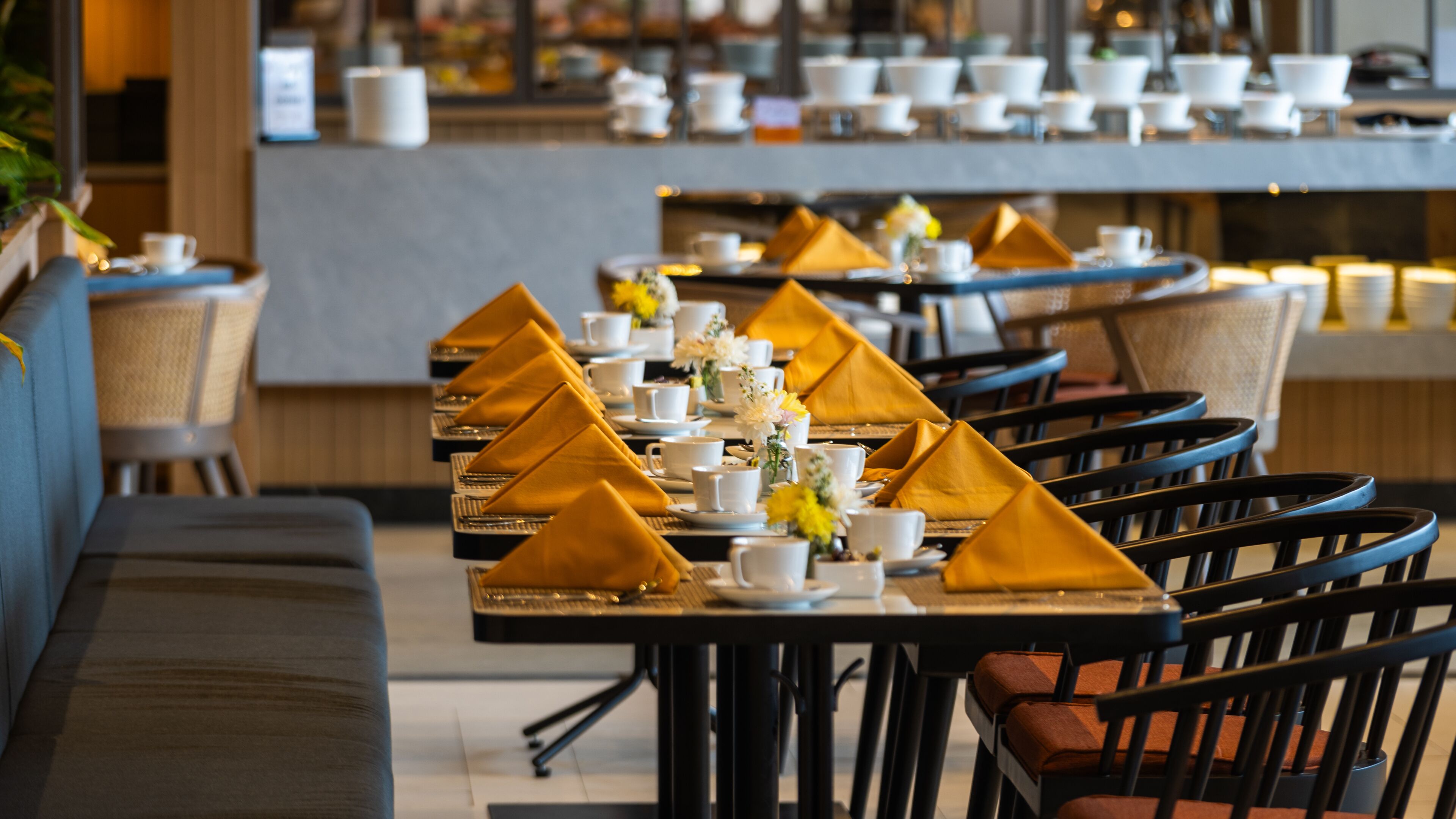 Restaurante com mesas preparadas para refeições, com guardanapos amarelos e louça branca.