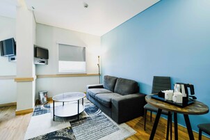 Uma sala de estar moderna com sofá, mesa de centro, TV e uma mesinha com chaleira e xícaras.