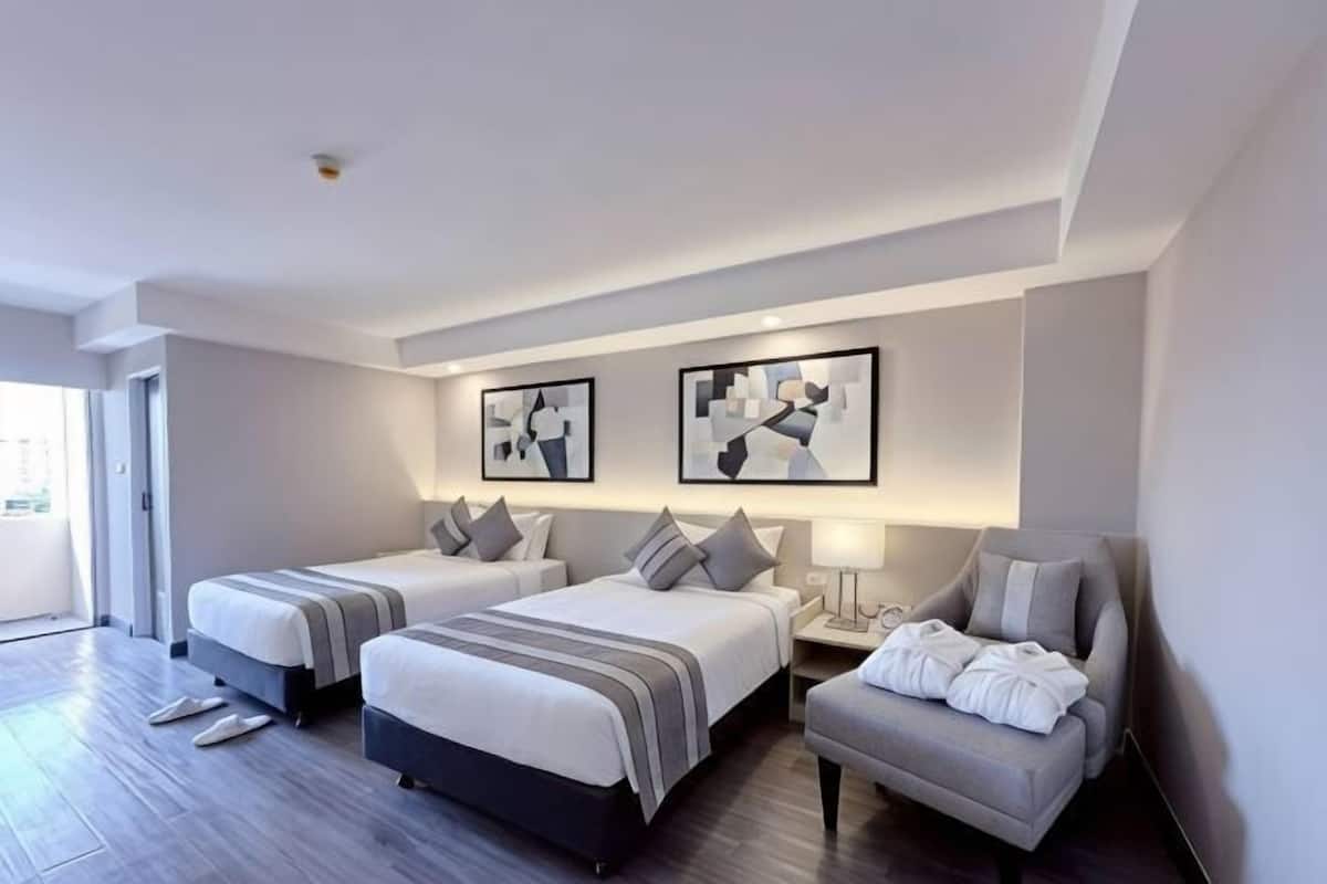 Quarto de hotel com duas camas, um sofá, uma escrivaninha e obras de arte na parede.