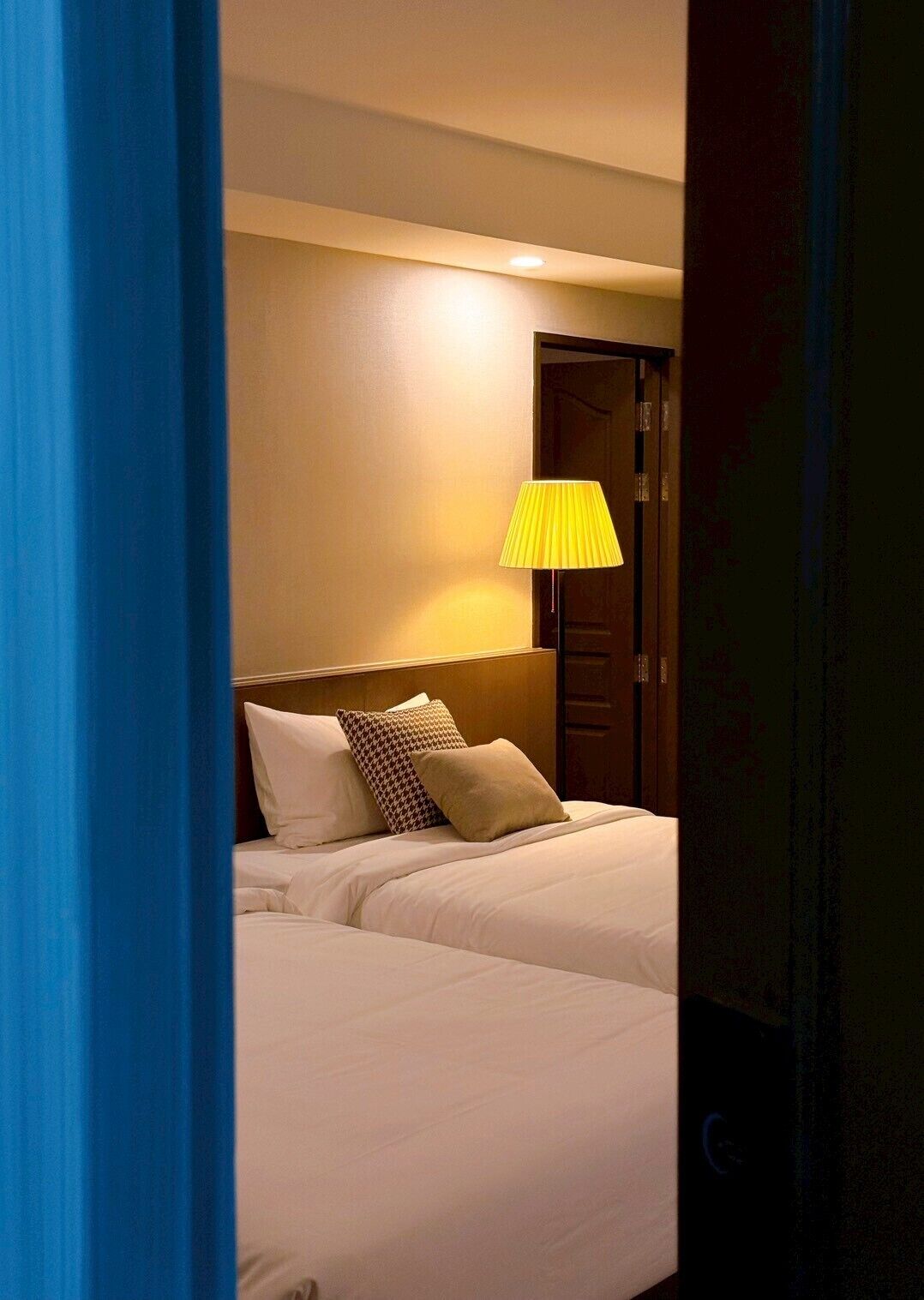 Quarto de hotel com cama, abajur e porta.