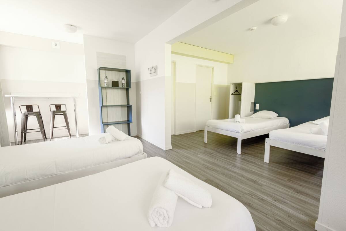Quarto de hotel com duas camas, uma escrivaninha, uma cadeira, uma estante e um guarda-roupa.