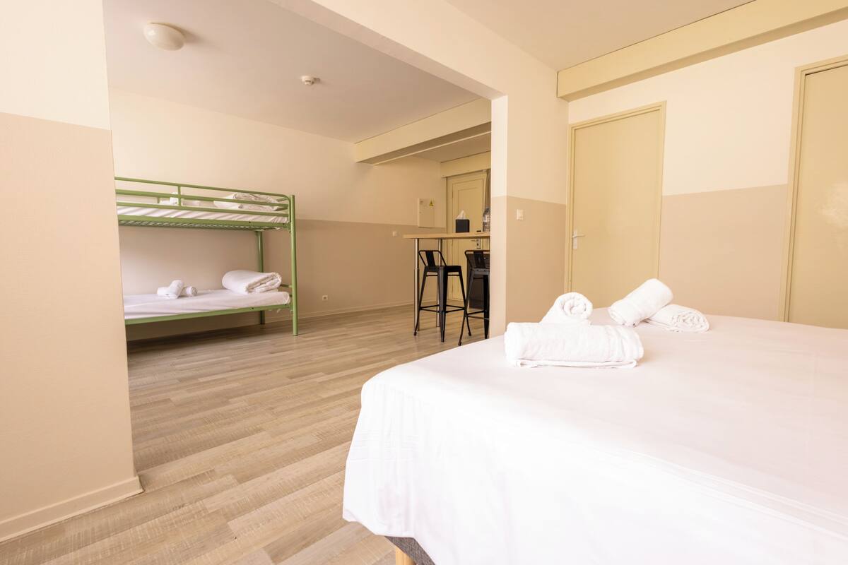 Quarto de hotel com beliche, uma escrivaninha e uma cadeira.