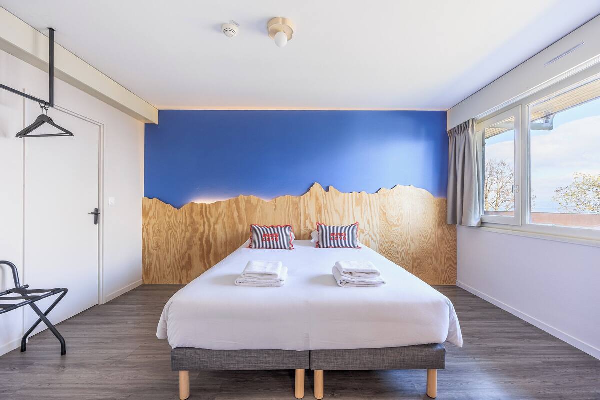 Quarto com cama, cabeceira de madeira, janela e luminária pendente.