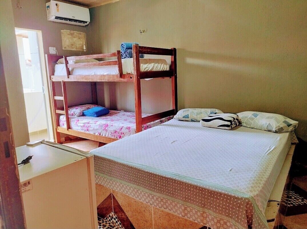 Quarto de dormitório com beliches, uma escrivaninha e uma cama com colcha estampada.