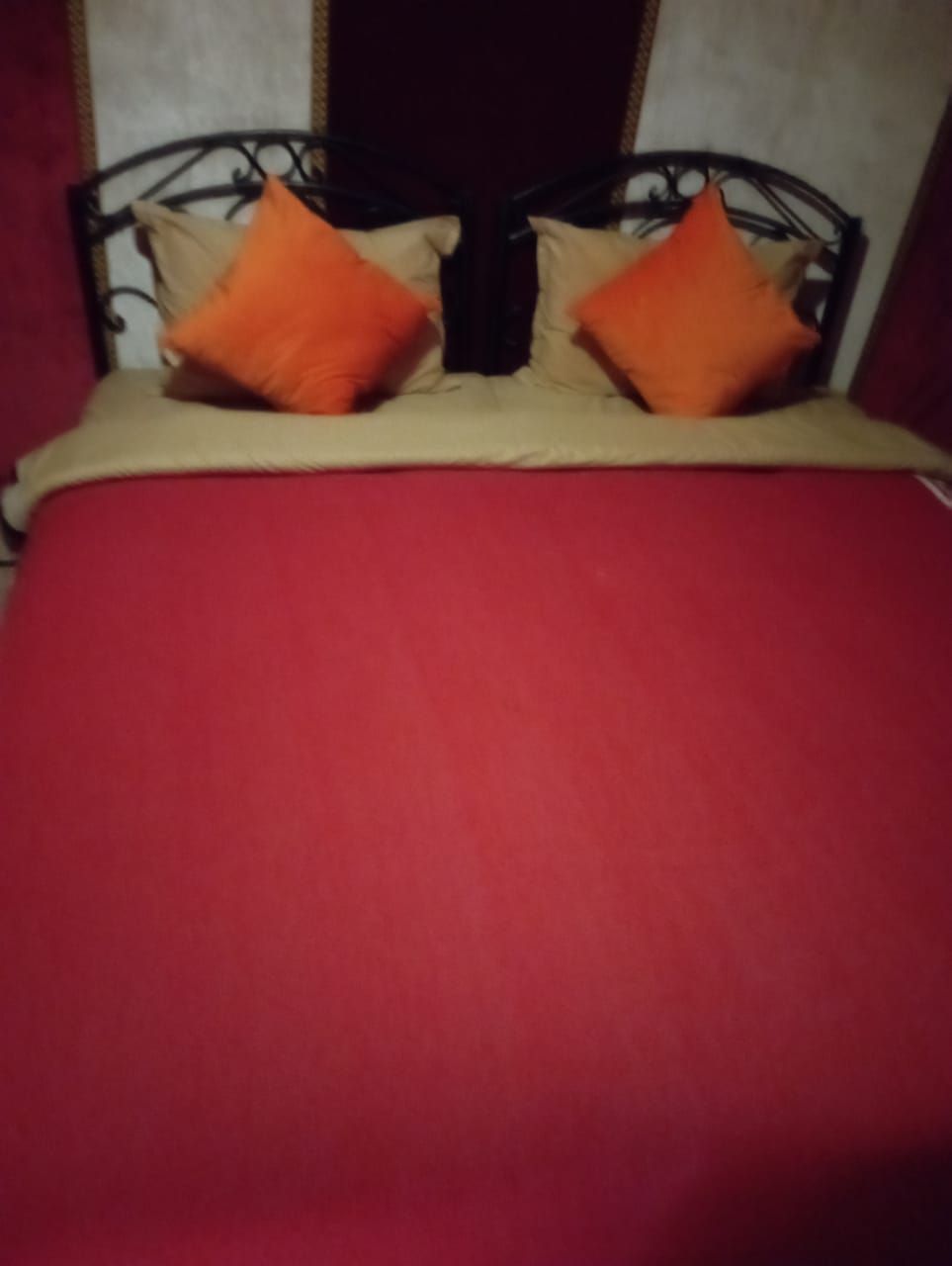 Uma cama com um cobre-leito vermelho e duas almofadas laranja.