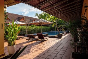 Uma área externa coberta com piscina, espreguiçadeiras e guarda-sóis.
