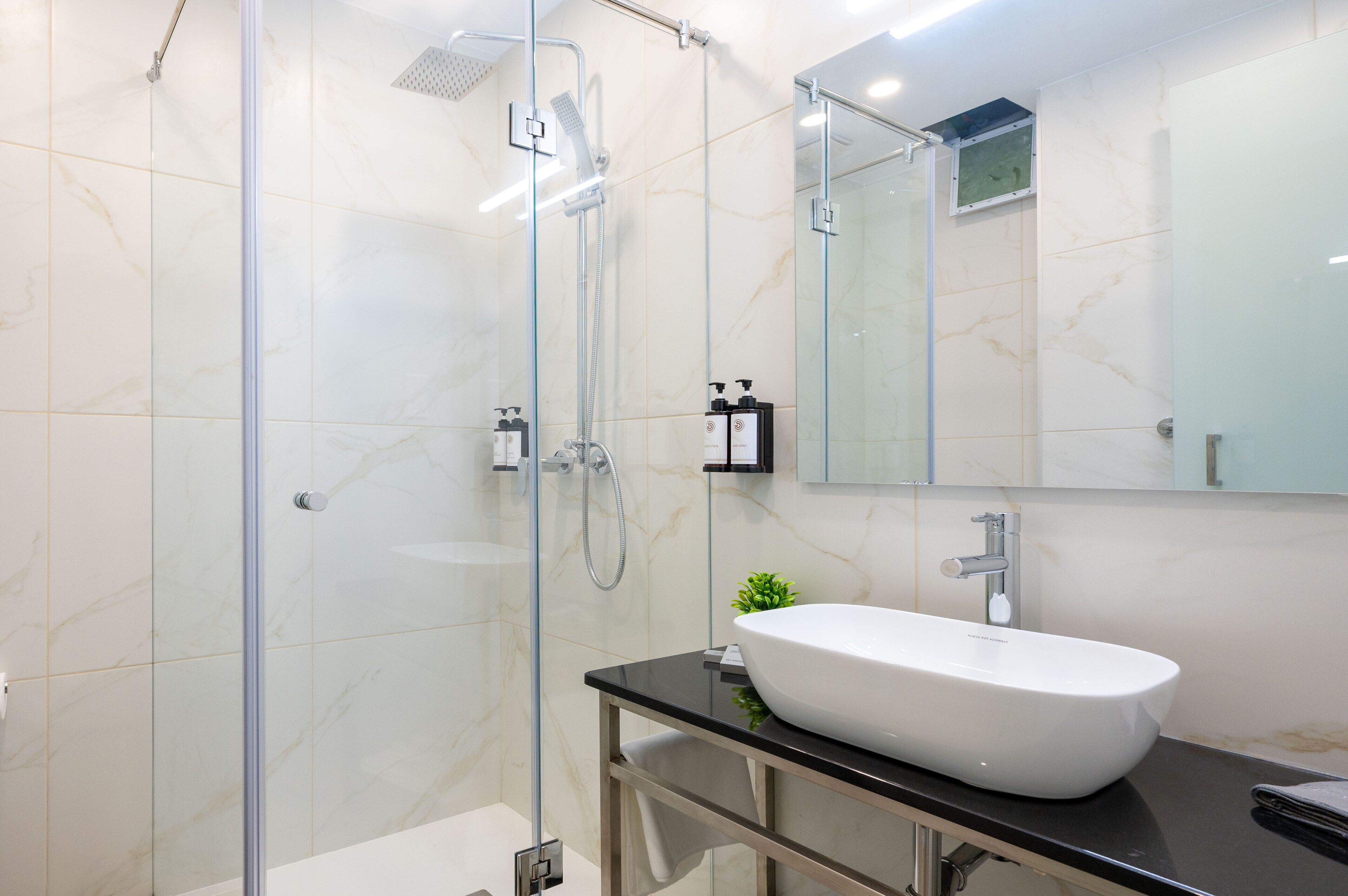 Uma casa de banho moderna com chuveiro em cabine de vidro, lavatório branco e espelho grande.