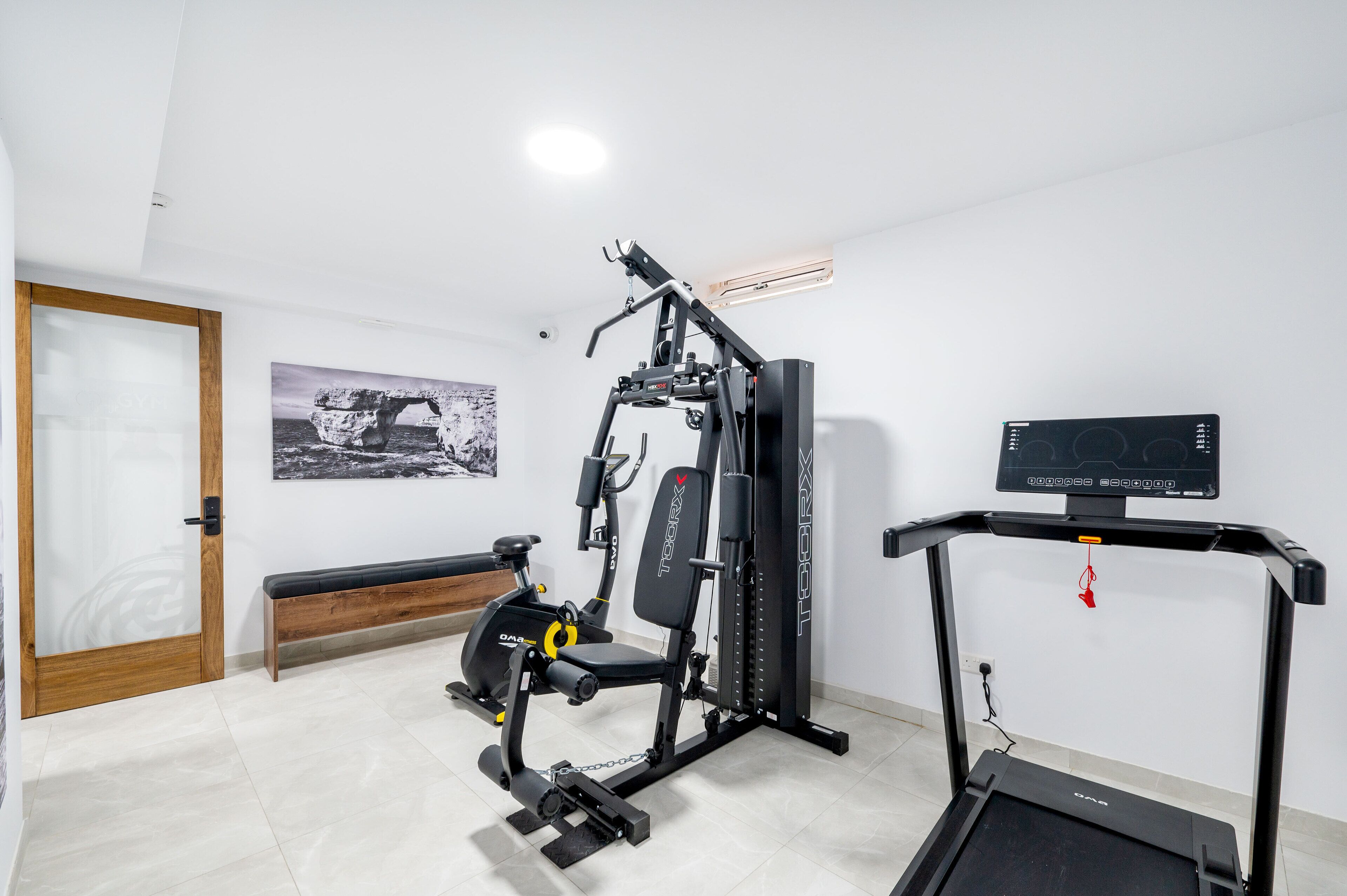 Uma academia em casa com esteira, equipamento de exercícios multifuncional e um banco.
