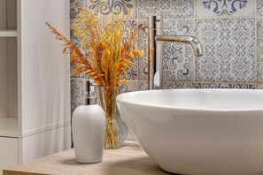 Um banheiro com uma pia branca, um vaso de vidro com flores secas e uma torneira.