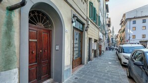 Uma rua estreita com carros estacionados de um lado e um edifício com uma porta de madeira grande e uma janela pequena.