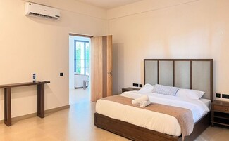 Quarto com cama, mesas de cabeceira, um banquinho e um aparelho de ar condicionado.