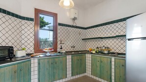 Uma cozinha com armários verdes, micro-ondas, torradeira, pia e janela com vista para árvores.