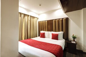 Quarto de hotel com cama grande, cabeceira de madeira, mesa de cabeceira e um vaso com planta.