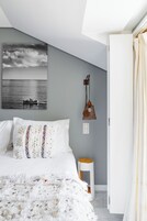 Quarto com uma cama, uma luminária na parede e um quadro de um barco.