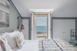 Um quarto com uma cama, vista para o mar, uma varanda e uma porta.