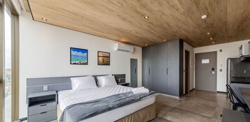 Quarto de hotel moderno com uma cama grande, escrivaninha e cozinha compacta.