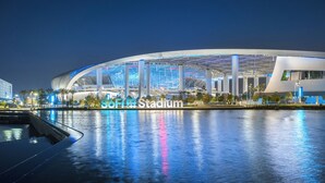 Um estádio moderno com uma grande placa iluminada com o nome 'SoFi Stadium' refletido na água.