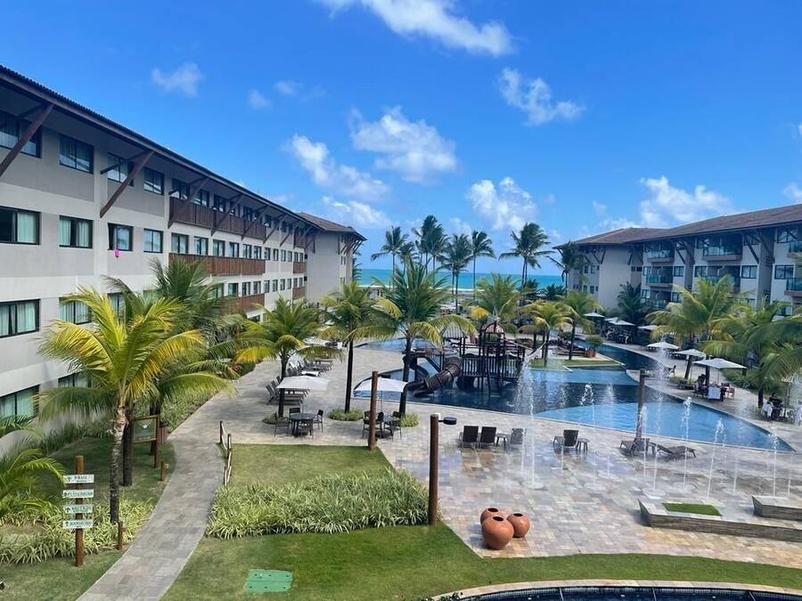 Um hotel com piscina, palmeiras e céu claro.