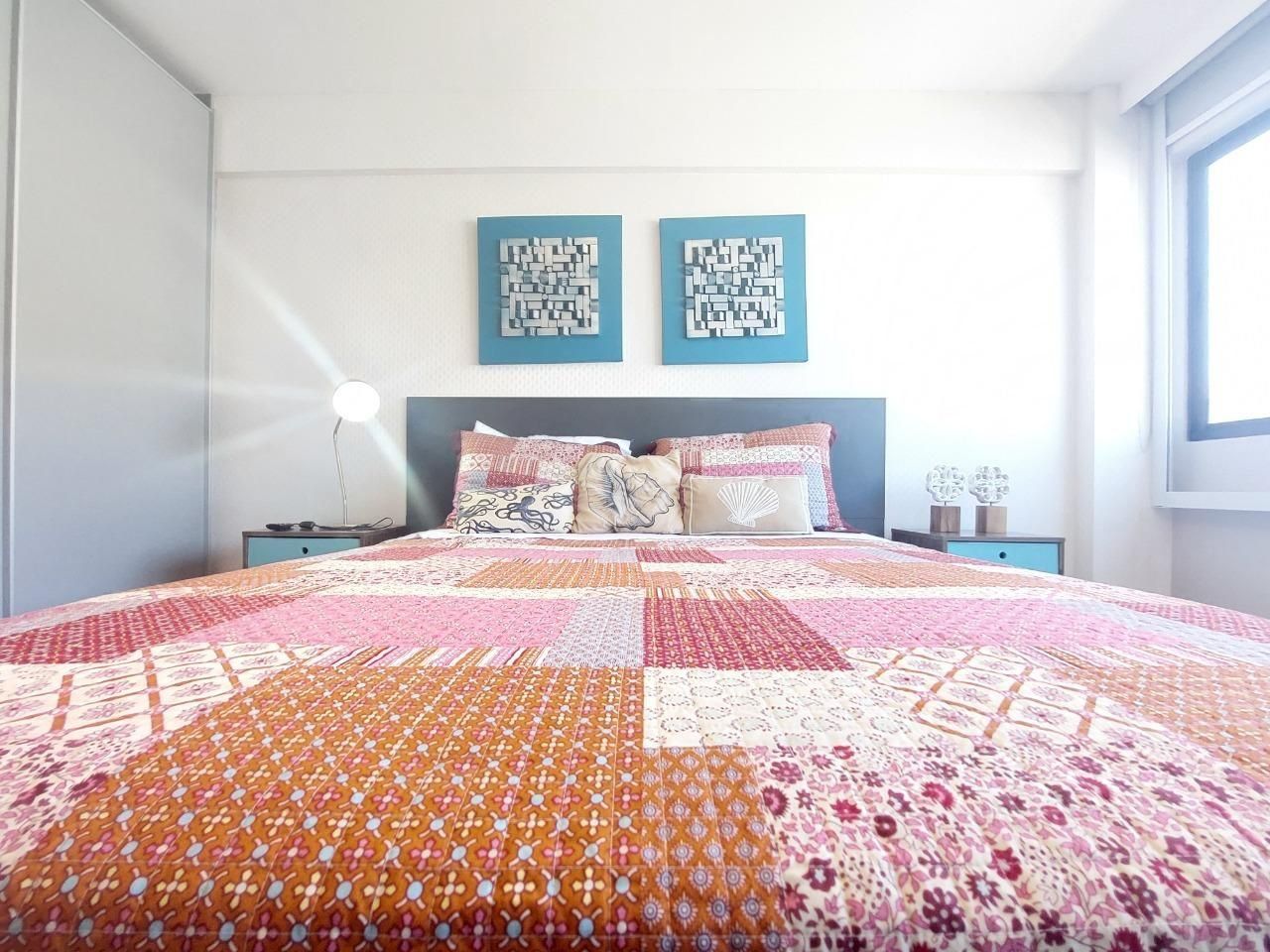 Quarto com uma cama grande, duas mesas de cabeceira, um criado-mudo, uma luminária na parede e duas obras de arte abstratas nas paredes.