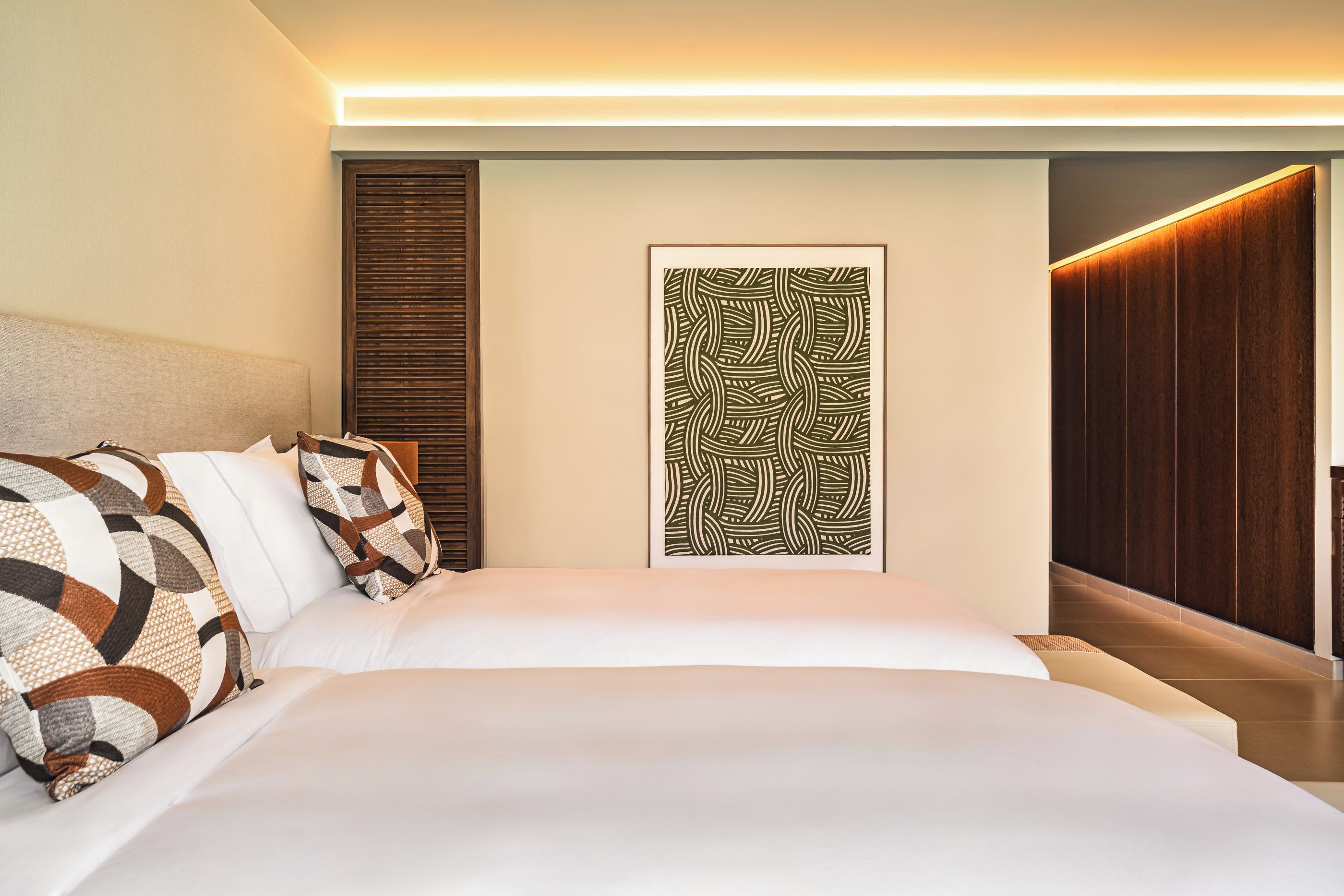 Quarto de hotel moderno com uma cama grande, cabeceira de madeira, obra de arte abstrata emoldurada e guarda-roupa de madeira.