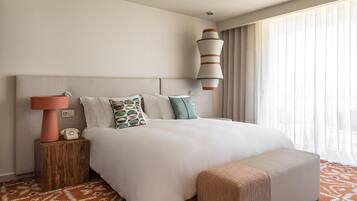 Quarto de hotel com uma cama grande, abajur, telefone e janela com cortinas.