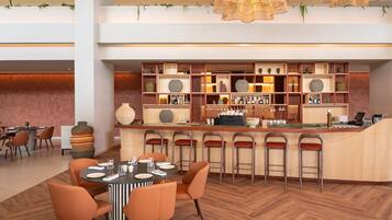 Uma área de bar moderna com uma mesa redonda central e vários bancos, rodeada por prateleiras com garrafas e objetos decorativos.
