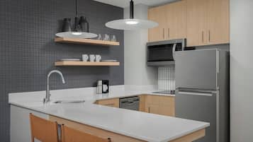 Uma cozinha moderna com bancada branca, eletrodomésticos de aço inoxidável, armários de madeira e lava-louças embutida.