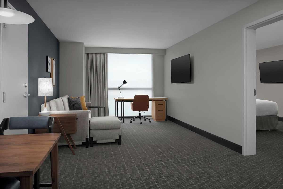 Quarto de hotel com sofá, escrivaninha, cadeira, cama e televisão.