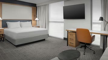 Quarto de hotel moderno com cama, escrivaninha, cadeira e grandes janelas.