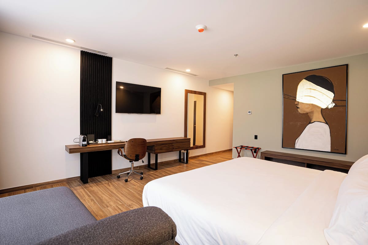 Quarto de hotel com uma cama grande, uma escrivaninha com cadeira, uma televisão e um quadro na parede.