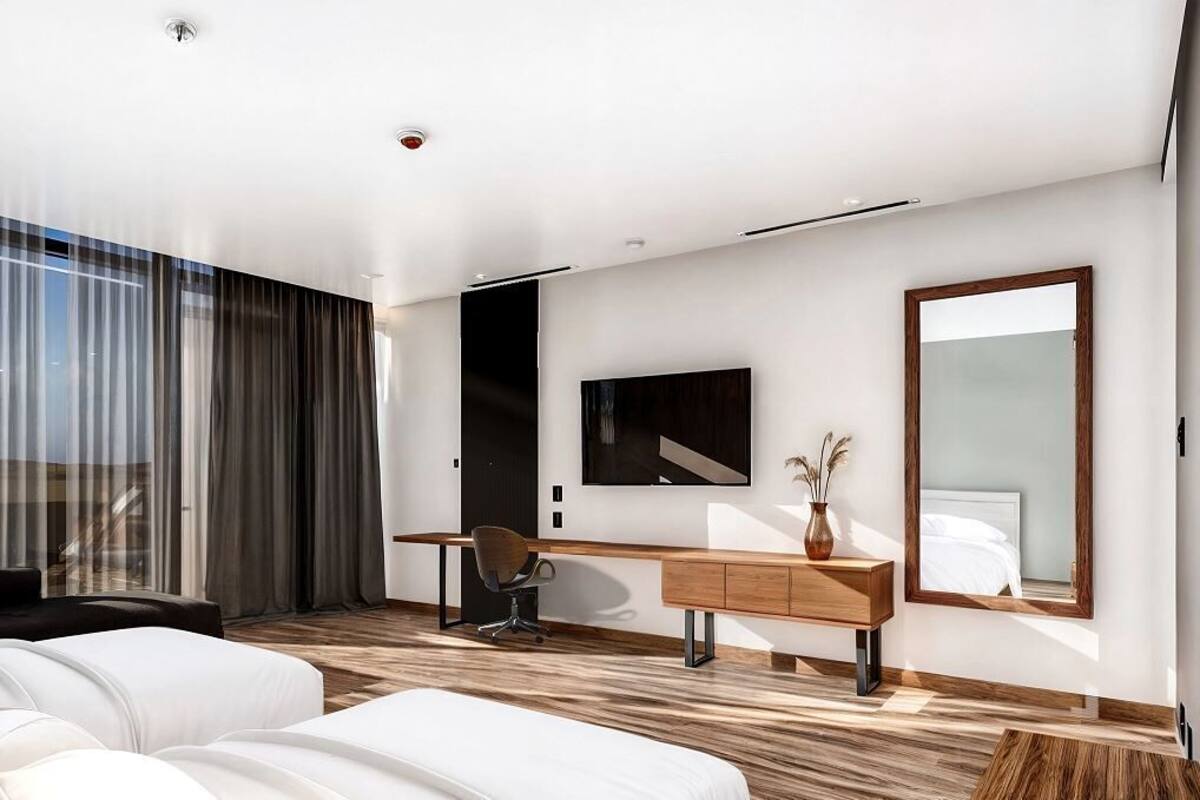 Quarto de hotel moderno com uma cama grande, uma escrivaninha, uma cadeira, uma TV e um espelho amplo.