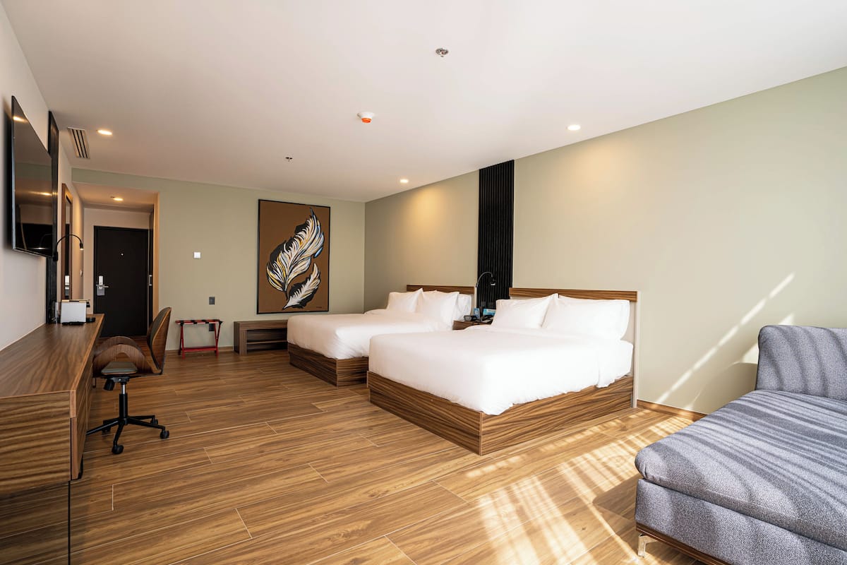 Quarto de hotel com duas camas, uma escrivaninha, uma cadeira e uma televisão.